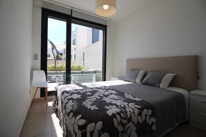 Quarto com cama, uma cadeira, mesa de cabeceira e uma janela grande.