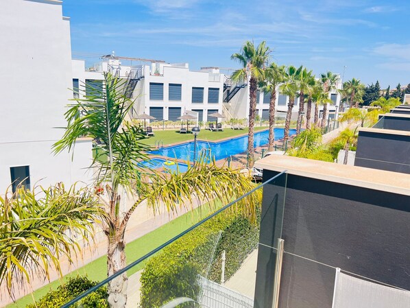 Um edifício moderno com piscina no terraço, rodeado por palmeiras e um céu azul límpido.