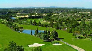 Um campo de golfe com lago, áreas de areia e vista ampla da paisagem circundante.