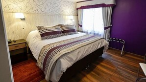 Quarto com cama, mesas de cabeceira, criados-mudos e uma janela com cortinas, além de uma parede com desenho estampado.