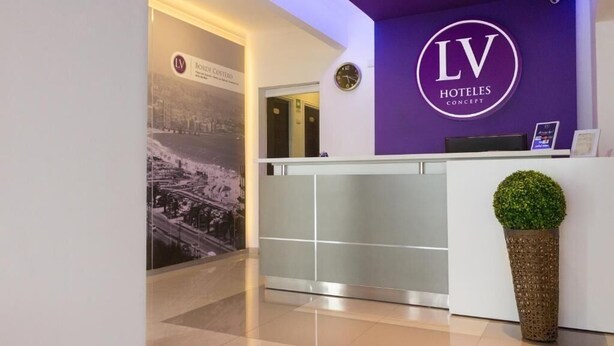 Uma área de recepção de hotel, com um balcão de recepção, um relógio e um cartaz na parede.