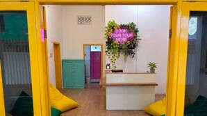 Uma área de recepção de hotel com um letreiro de neon, um balcão de atendimento, um sofá verde e um armário azul-esverdeado.