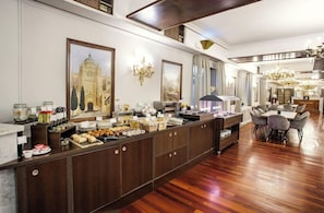 Um lobby de hotel com buffet, um candelabro e uma grande pintura de um edifício.