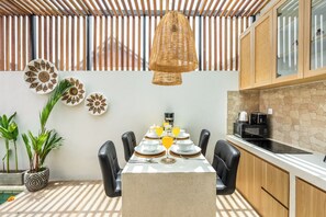 Uma sala de jantar com uma mesa posta para quatro pessoas, rodeada por cadeiras, e um lustre pendurado acima.