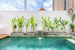 Piscina com cachoeira e fileira de bananeiras ao lado.