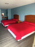 Quarto de hotel com duas camas, cabeceira de madeira, mesa de cabeceira e um espelho.
