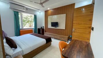 Quarto de hotel com cama, escrivaninha, cadeira, televisão e guarda-roupa.