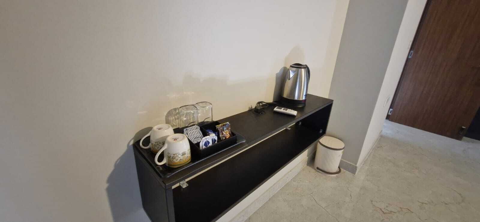 Um console preto com uma chaleira, duas canecas, um controle remoto e uma lixeira.