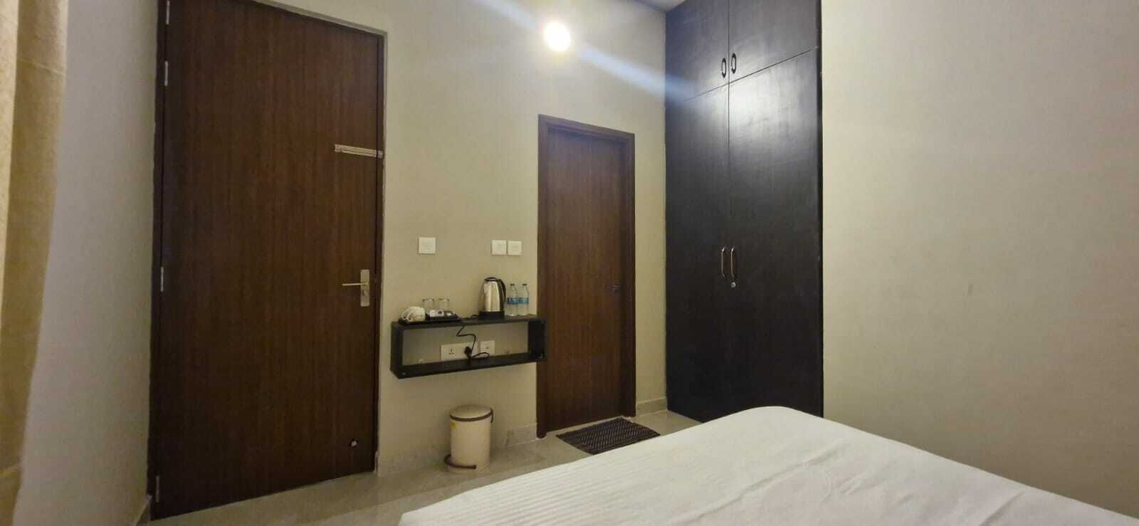 Quarto de hotel com cama, guarda-roupa, prateleira com produtos de higiene e um cesto de lixo.