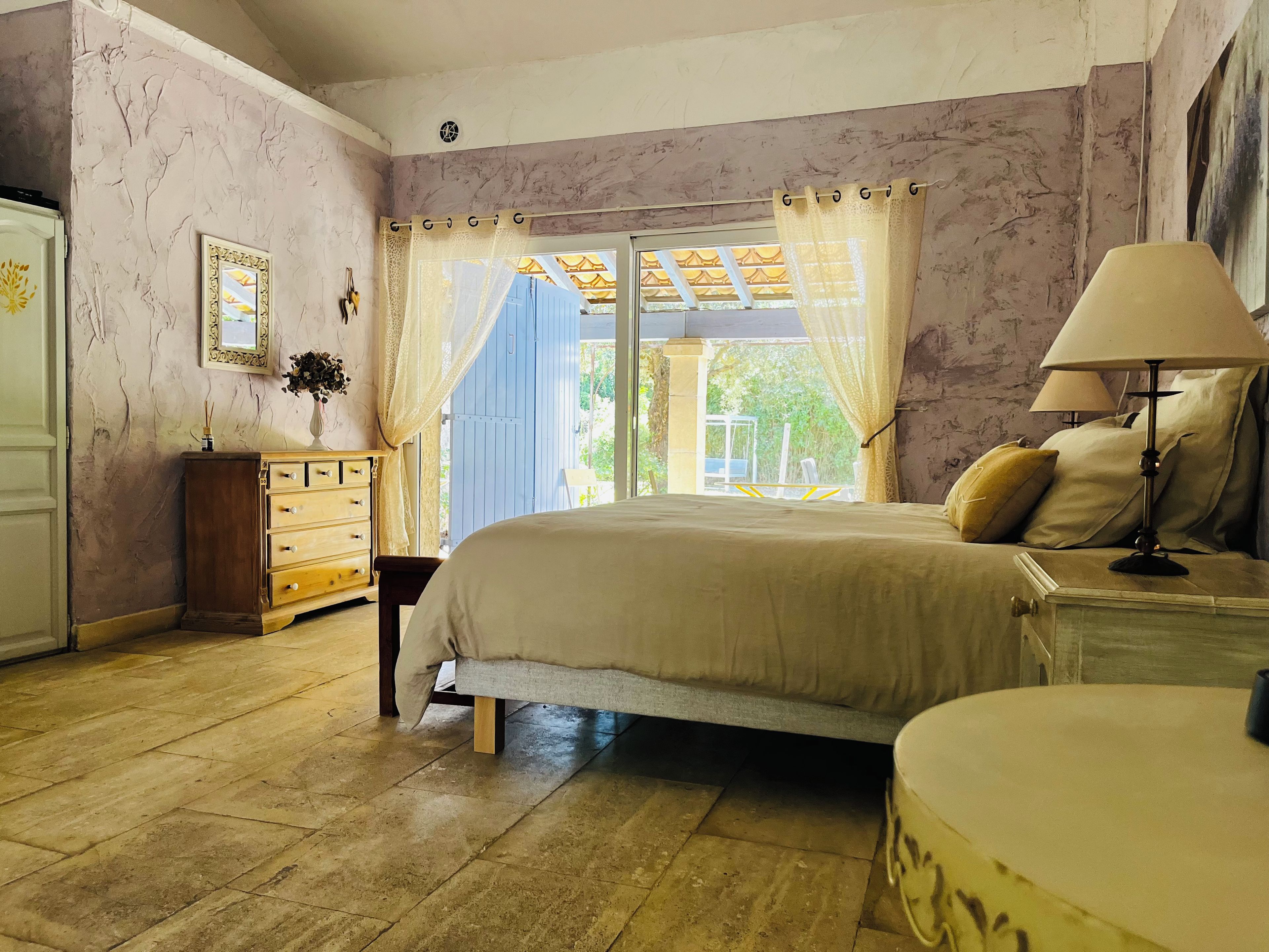 Quarto com cama, mesa de cabeceira, cômoda e janela com cortinas.