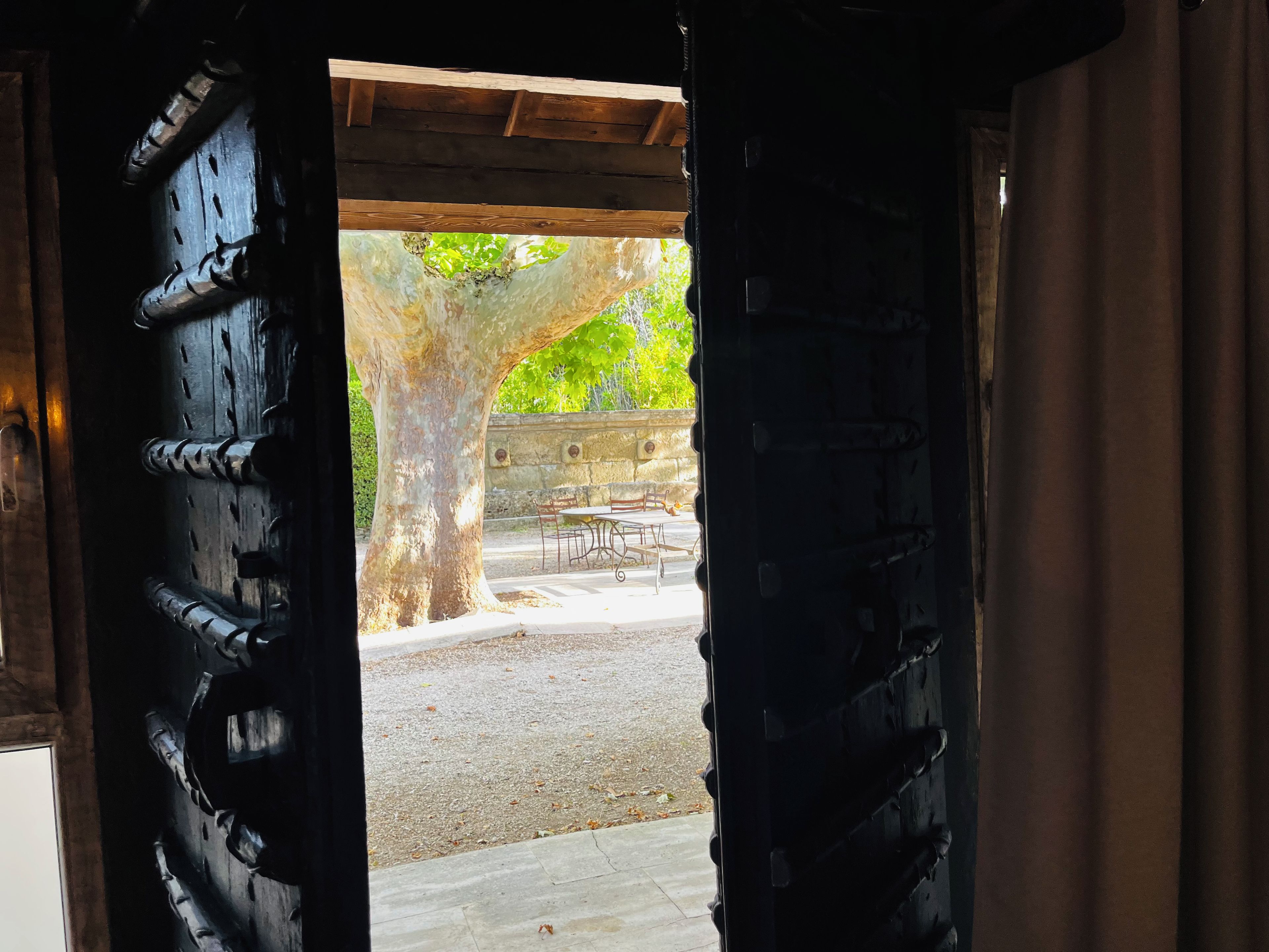 Abertura de porta que dá para área externa com muro de pedra, uma árvore e mesa com cadeiras.