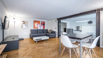 Uma sala de estar moderna com um sofá cinzento, uma mesa de centro e uma área de refeições com cadeiras brancas.