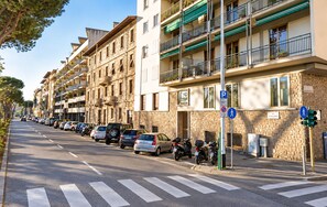 Rua com edifícios residenciais altos, carros estacionados e faixa de pedestres.