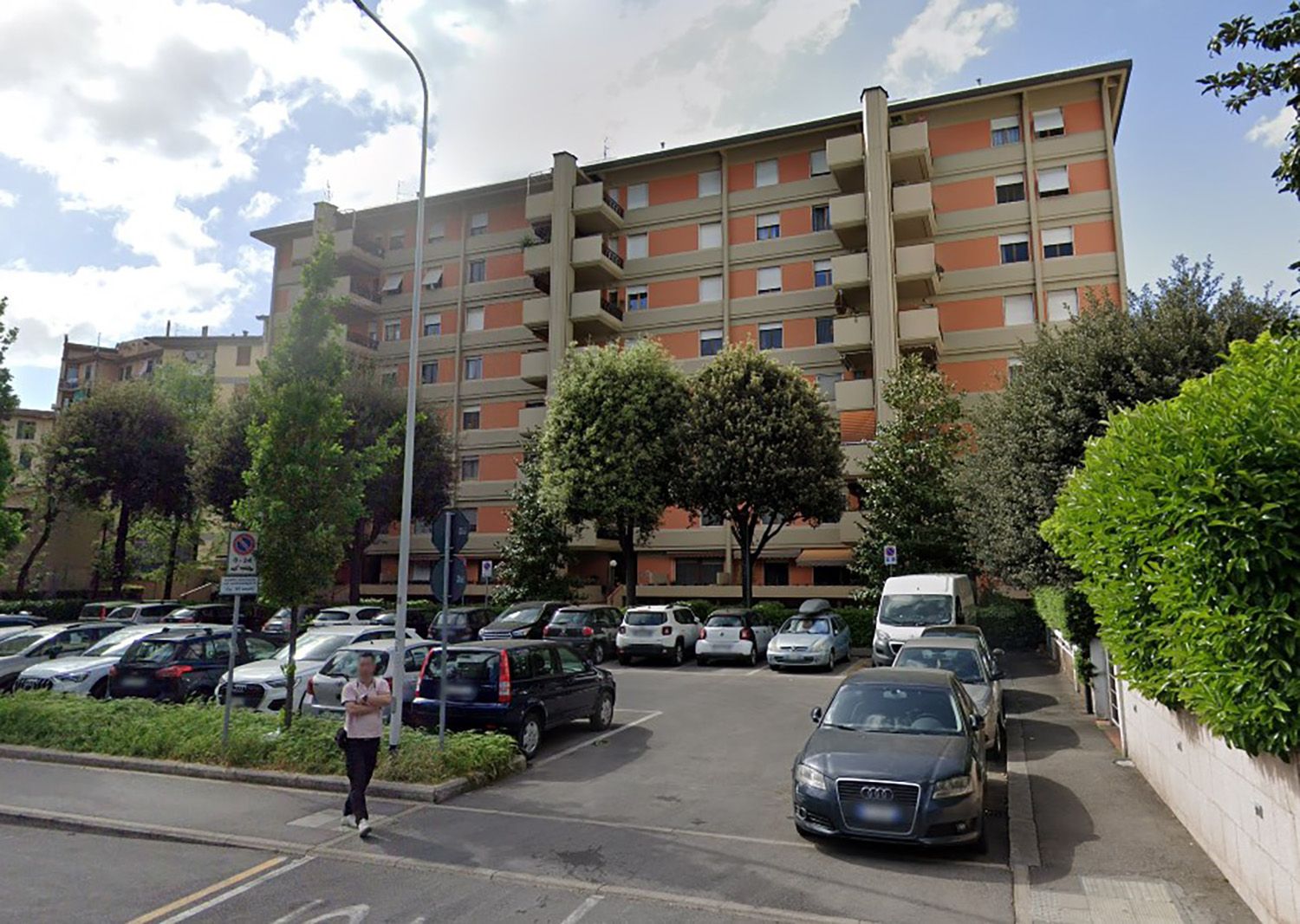 Edifício residencial com vários andares e estacionamento em frente.