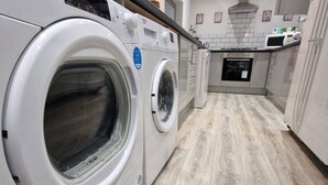 Uma área de lavanderia com máquina de lavar e secadora frontais, micro-ondas e uma pequena cozinha equipada com micro-ondas e torradeira.