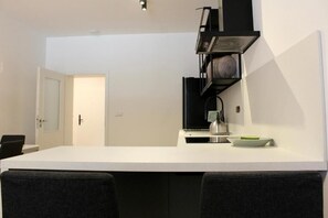 Uma cozinha moderna com bancada branca, prateleiras pretas e uma porta que dá para outro cômodo.