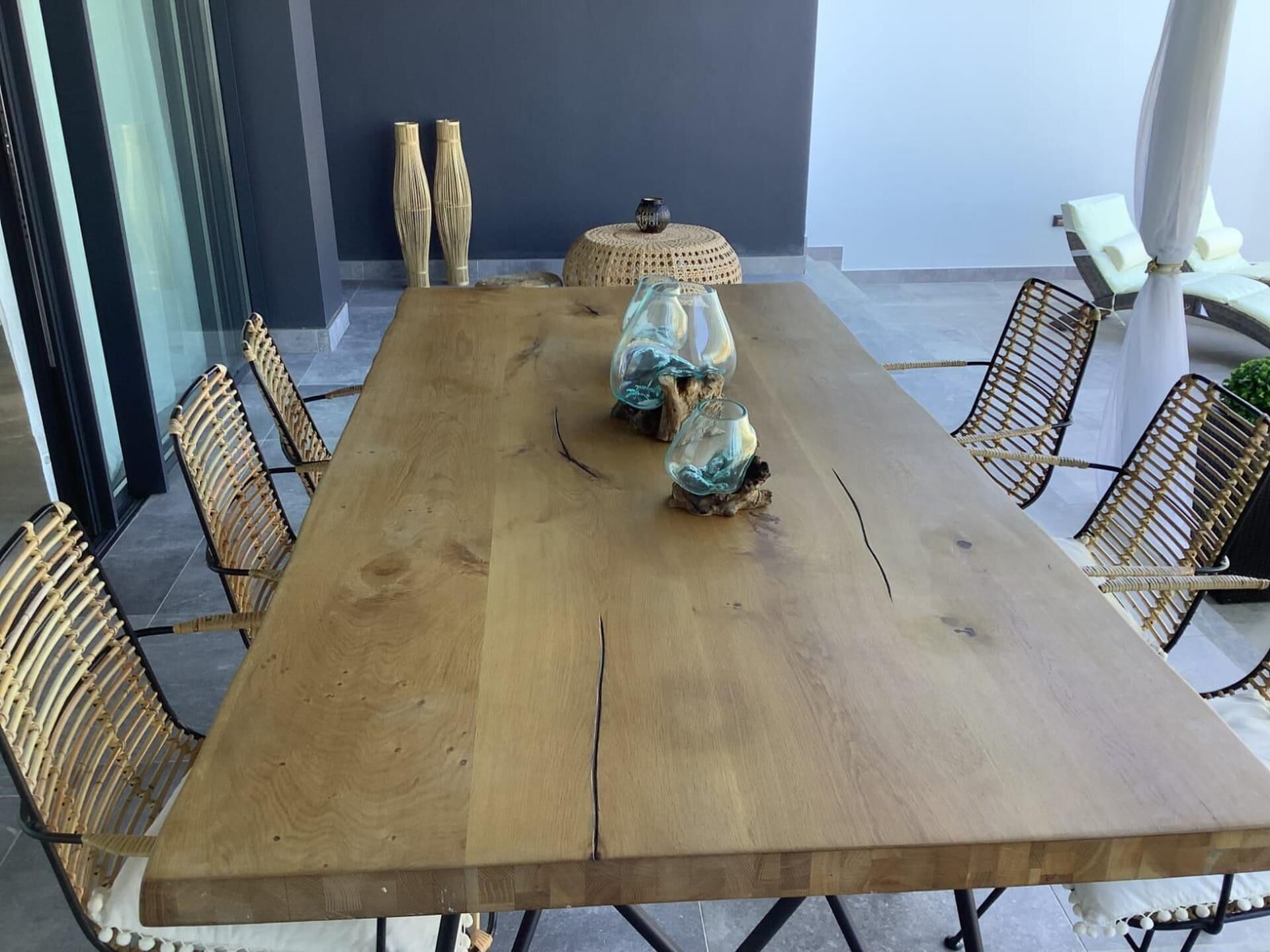 Uma mesa de jantar de madeira com cadeiras trançadas, um banquinho trançado e vasos de vidro com tecido azul.