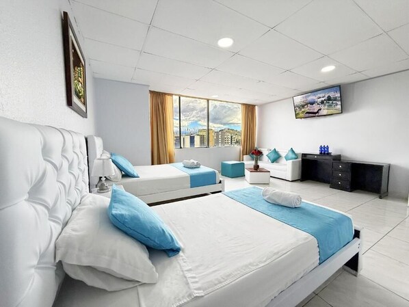 Quarto de hotel com duas camas, televisão, secretária e janela com vista para a cidade.
