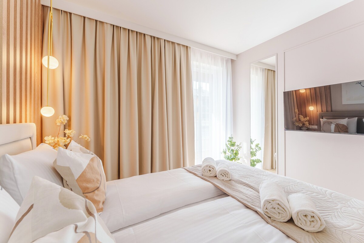Quarto de hotel com cama, cortinas, espelho e luminária pendente.