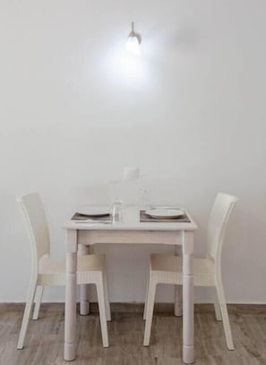 Uma mesa de jantar branca com duas cadeiras, um candeeiro sobre a mesa e uma pequena mesa com uma chávena e pires.