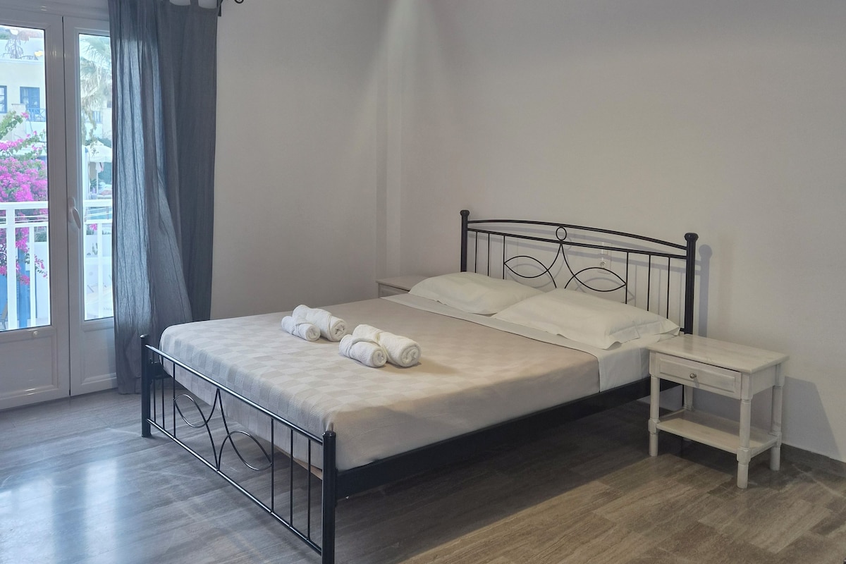 Quarto com cama, mesa de cabeceira e janela com cortinas.