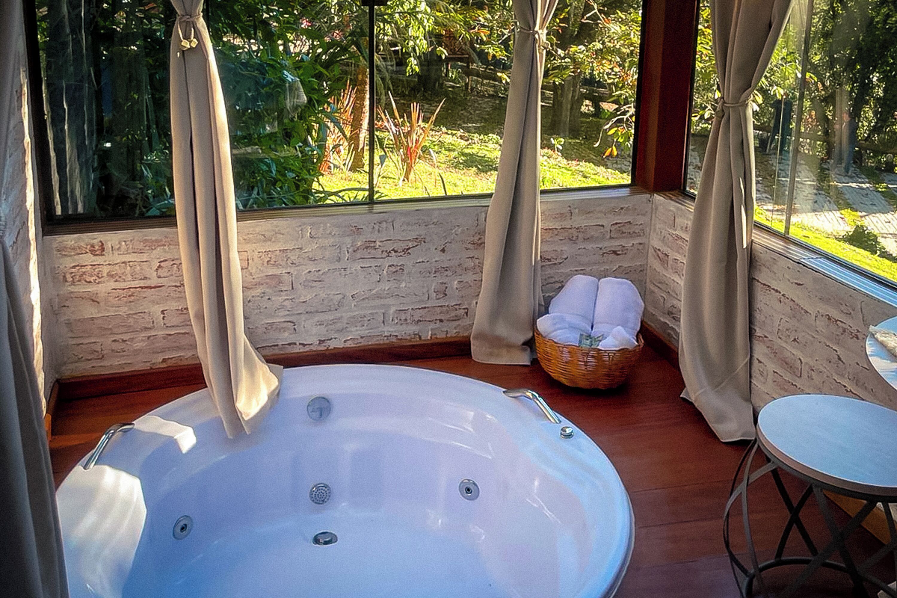 Um quarto de spa com uma banheira grande, uma cesta de vime com toalhas e uma pequena mesa.