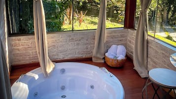 Um quarto de spa com uma banheira grande, uma cesta de vime com toalhas e uma pequena mesa.