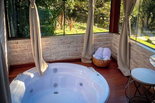 Um quarto de spa com uma banheira grande, uma cesta de vime com toalhas e uma pequena mesa.