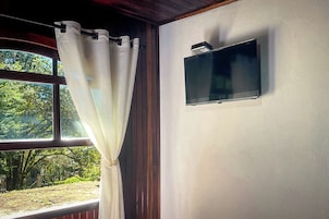 A room with a window, white curtains, and a mounted television on the wall.