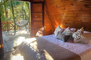 Quarto de cabana de madeira com cama, almofadas e vista para o exterior.