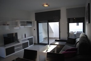 Uma sala de estar moderna com televisão de tela plana, uma porta de vidro que dá para uma varanda e um sofá.