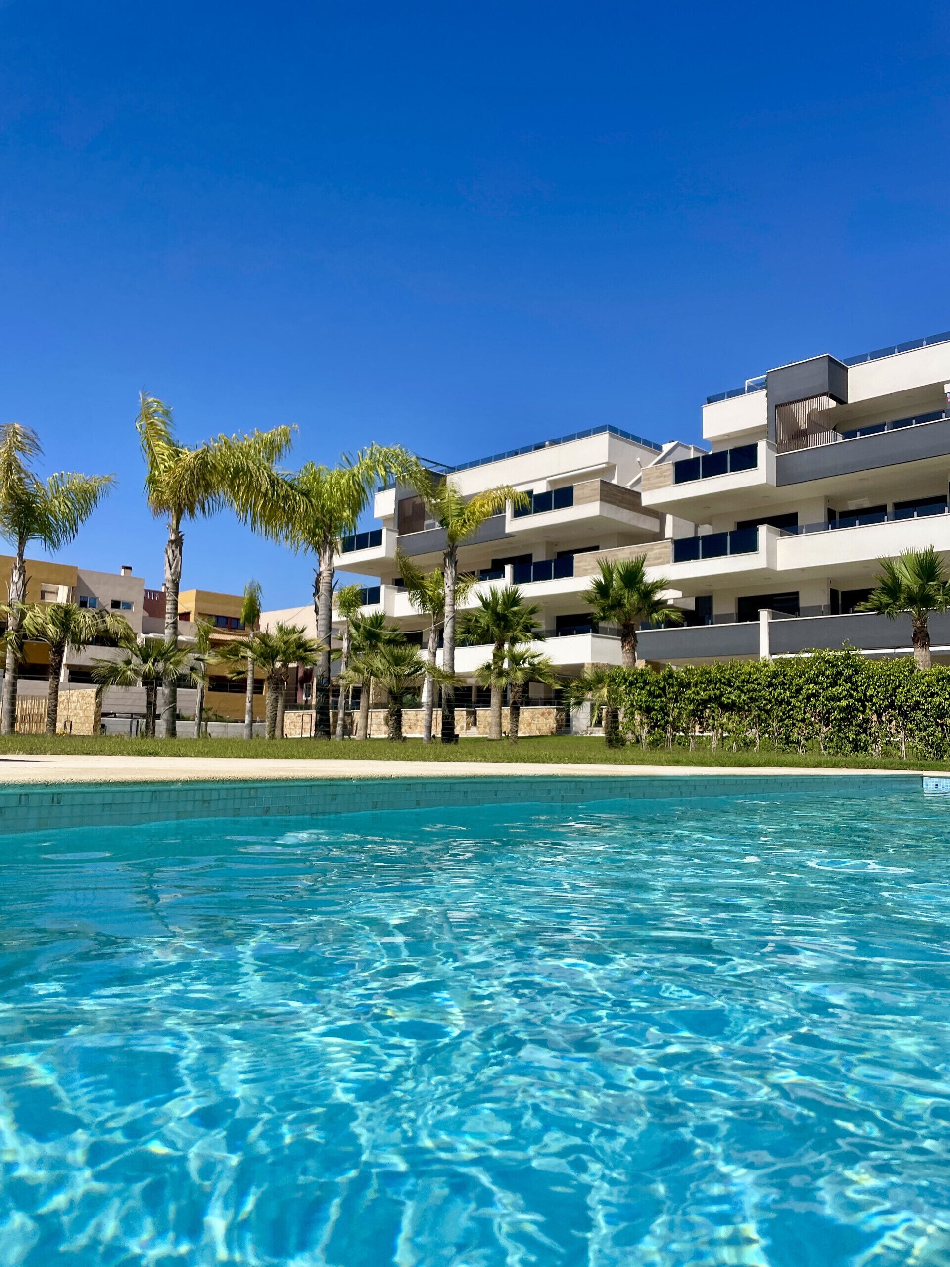Um hotel moderno com piscina, palmeiras e um céu azul límpido.