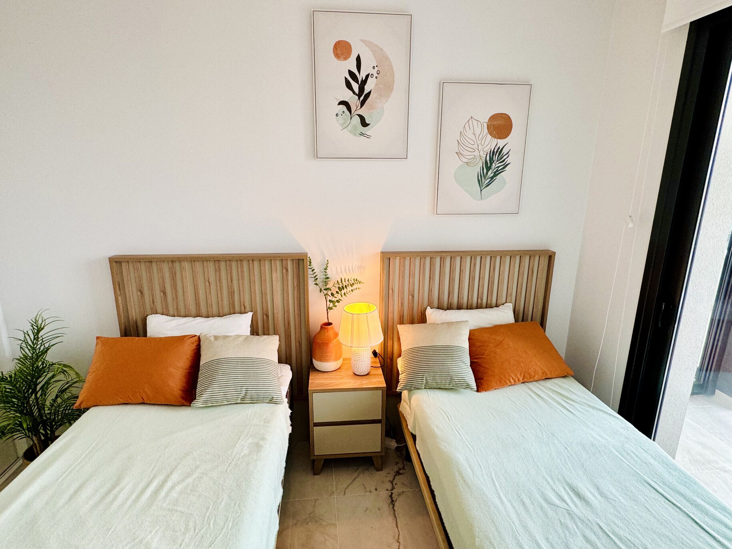 Quarto de hotel com duas camas, uma mesa de cabeceira com abajur e duas obras de arte penduradas na parede.