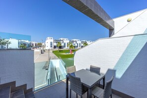 Um edifício moderno com varanda de vidro que dá para um parquinho e área residencial.