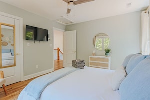 Quarto com uma cama, televisão, espelho e escada que leva a outro cômodo.