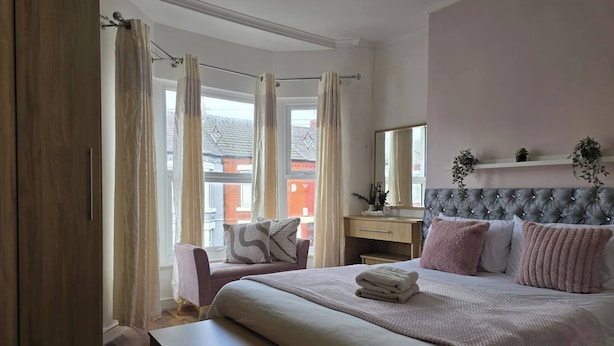 Quarto com cama, mesa de cabeceira, banqueta e vista para o exterior.