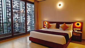 Quarto de hotel com cama grande, luminárias de cabeceira, mesa de cabeceira e vista através de uma janela com padrão.