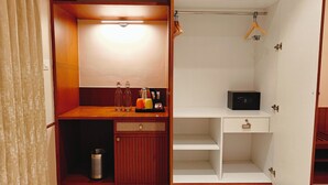 Quarto compacto e bem iluminado, com toucador de madeira, pia pequena e prateleira com um rádio.