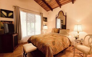 Quarto com cama, escrivaninha, cadeira, espelho e janela com cortinas.