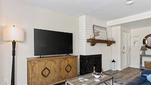 Uma sala de estar com televisão de tela plana, lareira, um armário de madeira e uma mesa de centro com livros e uma tigela.