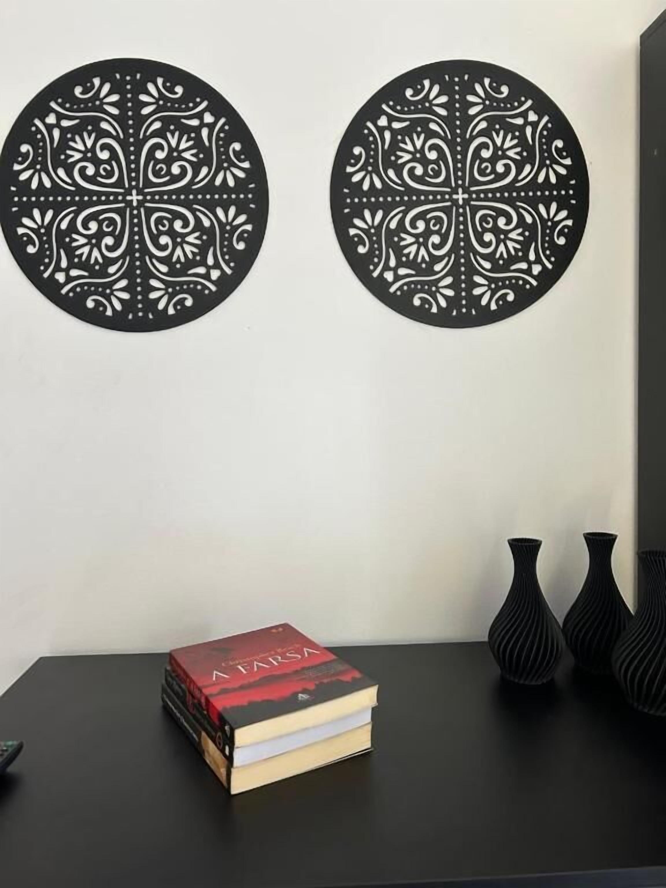 Um quarto com uma mesa preta, uma pilha de livros, três vasos pretos e duas peças decorativas na parede.