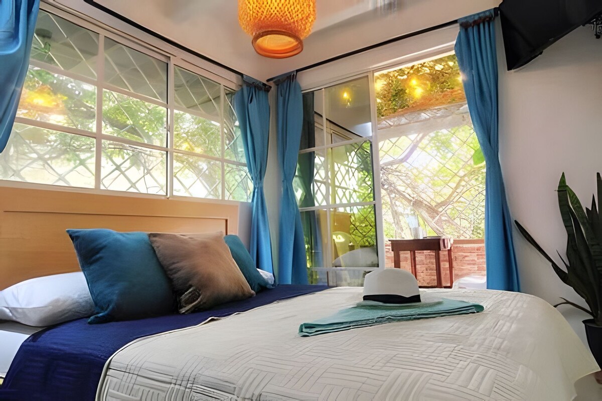 Quarto com uma cama grande, cabeceira de madeira e vista para o verde lá fora.