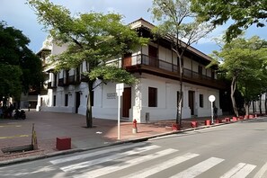 Um edifício de dois andares com fachada branca, varandas de madeira e um andar térreo de tijolos vermelhos.