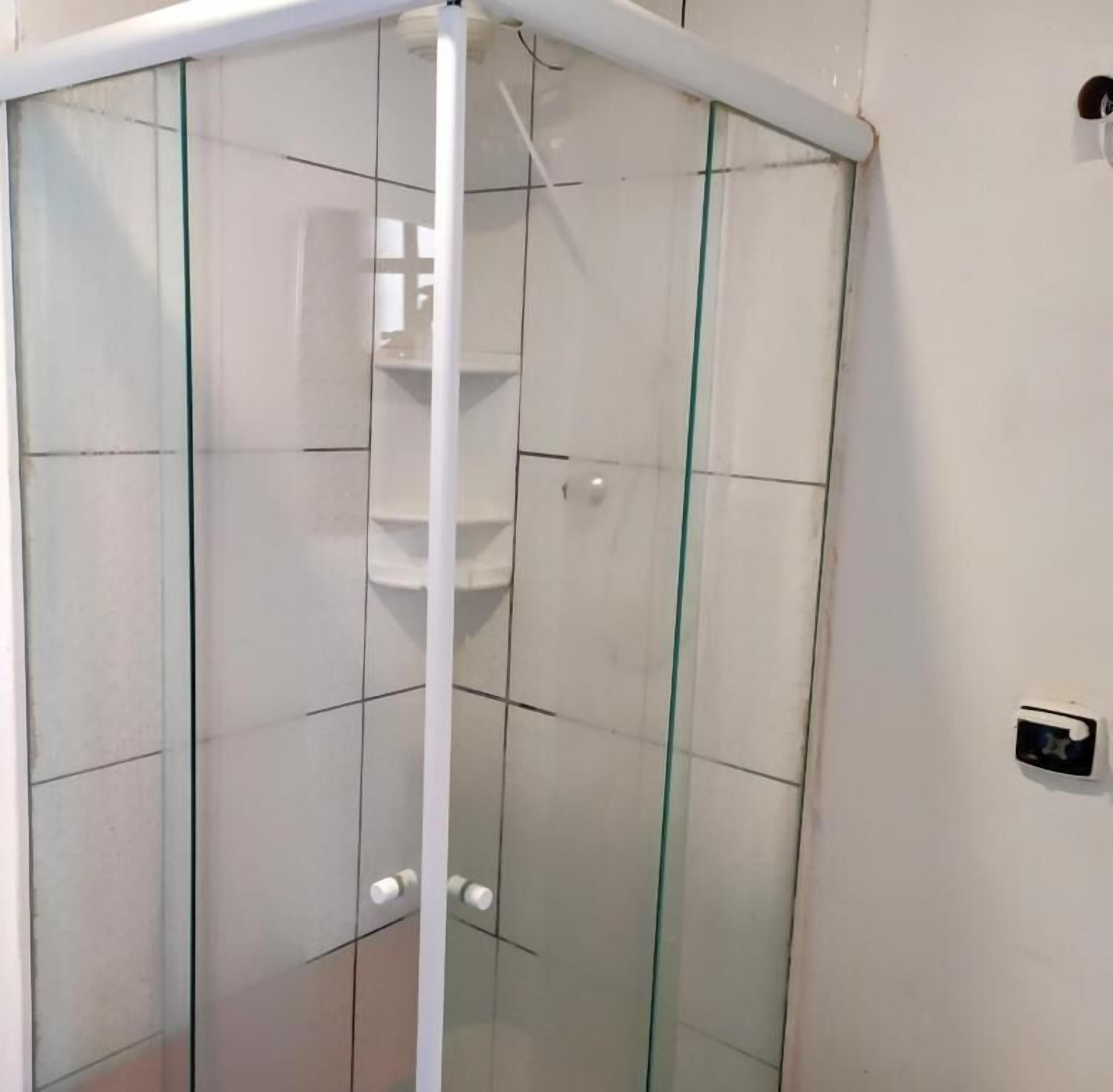 Box de chuveiro no canto com porta de vidro e moldura branca.