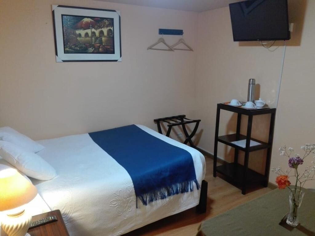 Quarto de hotel com uma cama, uma mesa de cabeceira, uma TV fixada na parede e um quadro pendurado acima da cama.
