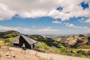 Um edifício moderno com telhado inclinado, rodeado por terreno acidentado e vegetação escassa.