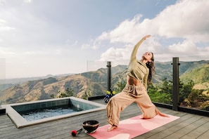 Uma pessoa praticando yoga em um deck de madeira, com vista para montanhas.