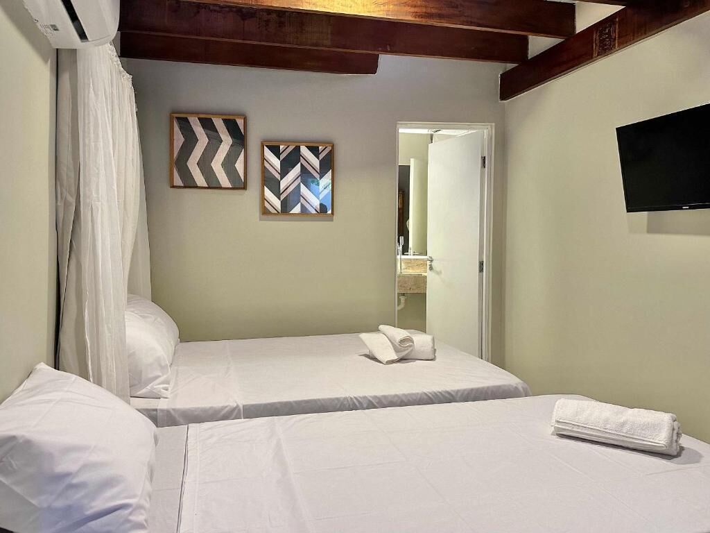 Quarto de hotel com duas camas, uma televisão de tela plana e duas obras de arte penduradas na parede.