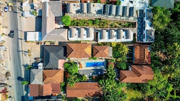 Vista aérea de um resort com diversas acomodações no estilo bangalô, uma piscina central e vegetação tropical exuberante.