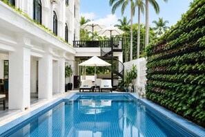 Piscina com deck revestido, rodeada por vegetação exuberante e palmeiras.